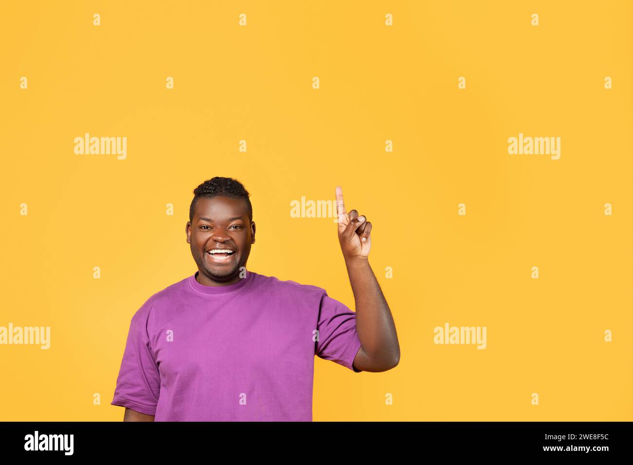 African guy with one arm raised pointing upwards, yellow backdrop Stock ...
