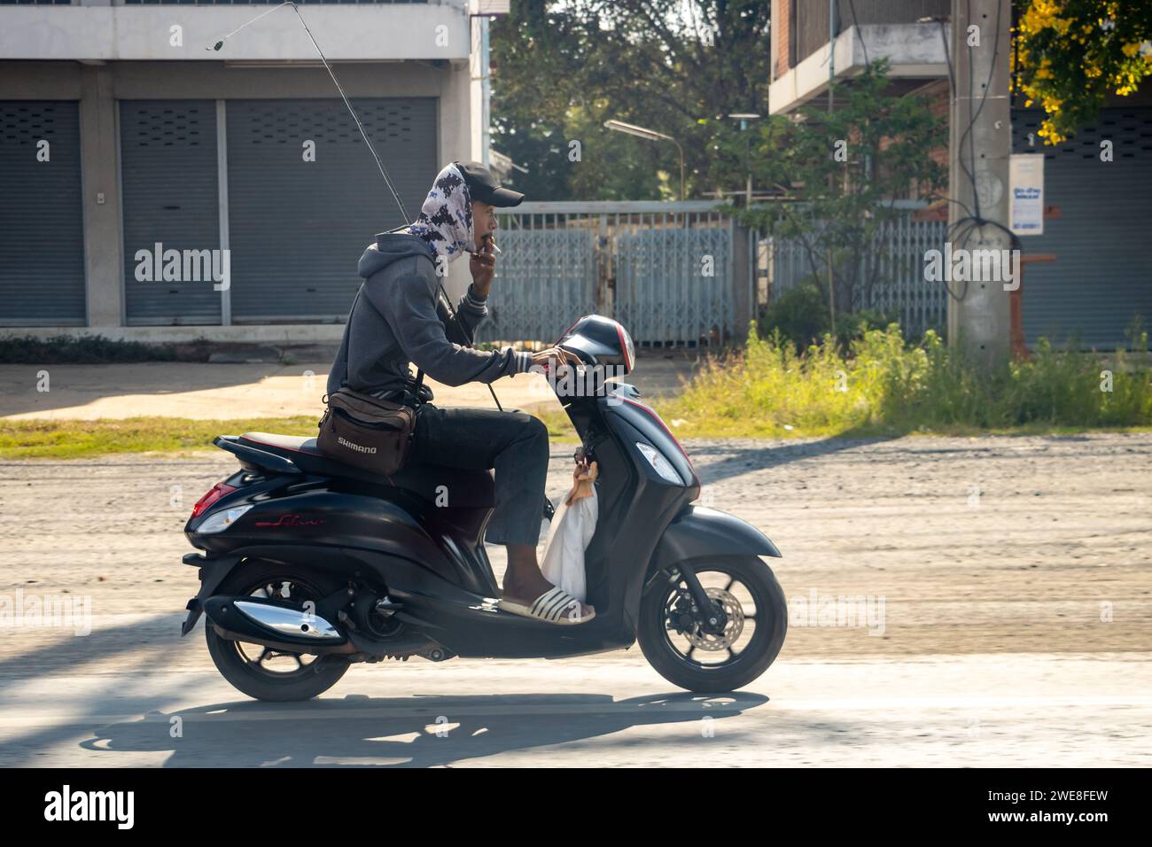 THAILAND, DEC 10 2023, A man with fishing rod rides a motorcycle and ...