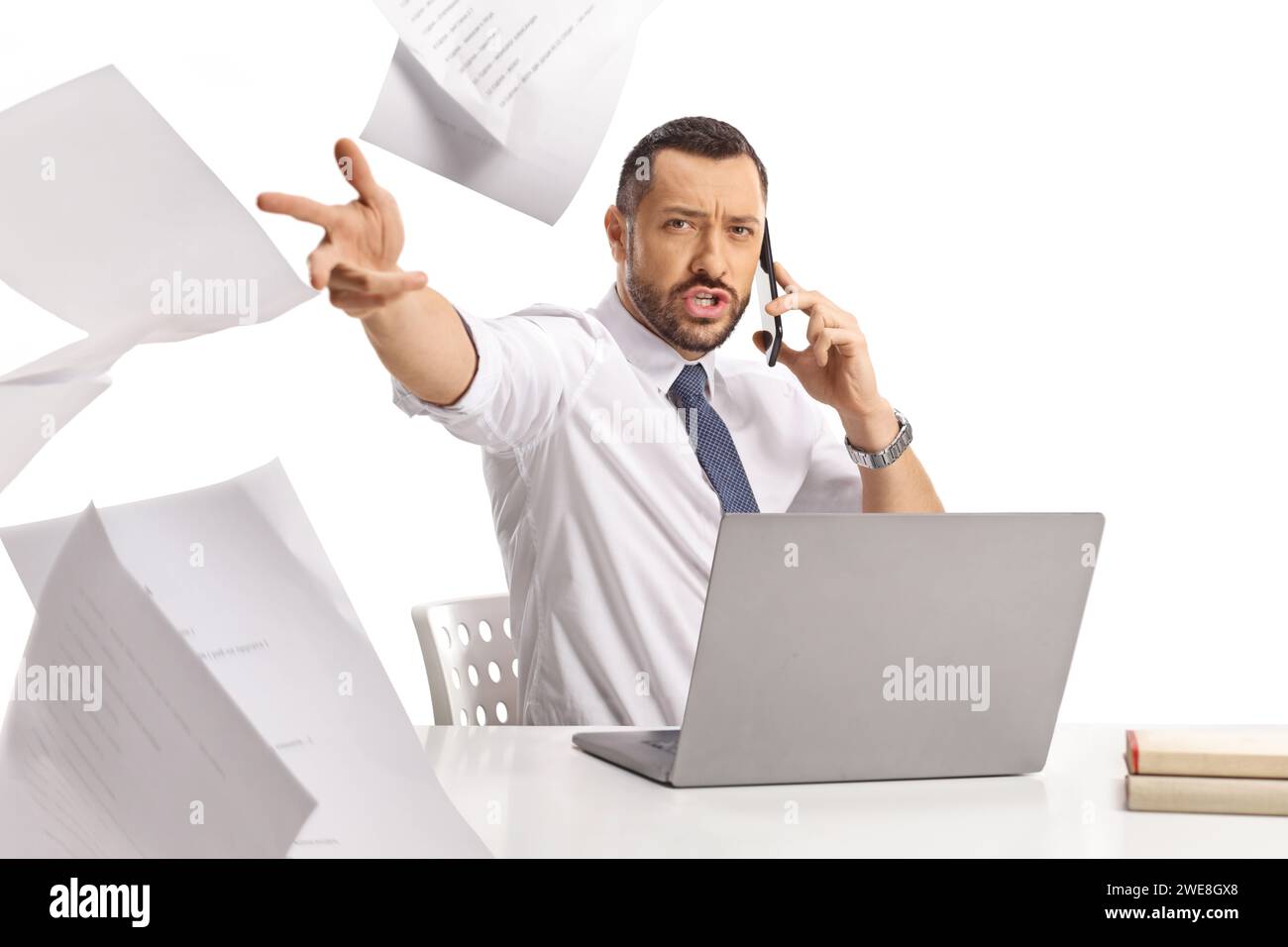 Angry businessman at a desk throwing papers and making a phone call ...