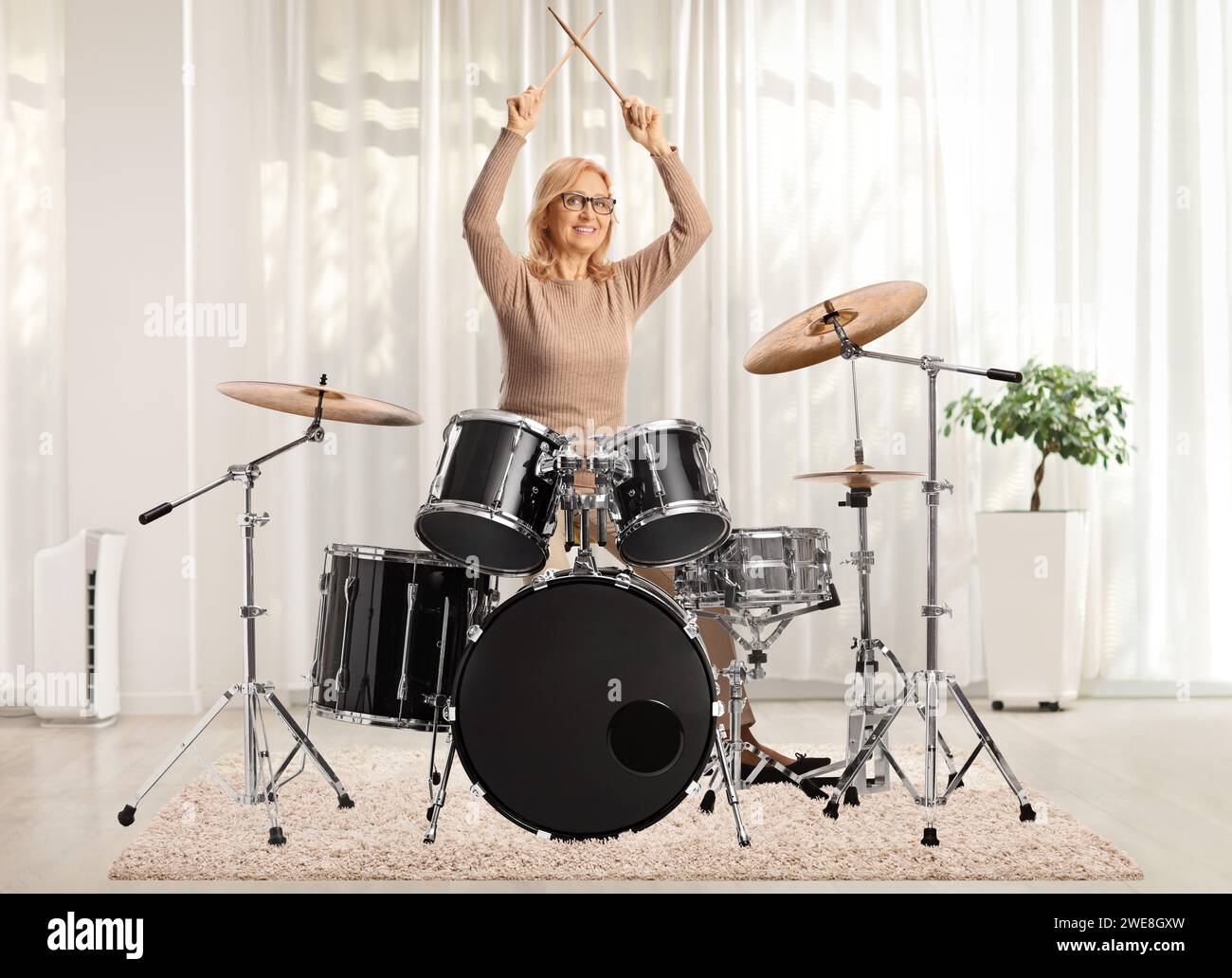 Middle aged woman playing the drums in a room Stock Photo - Alamy