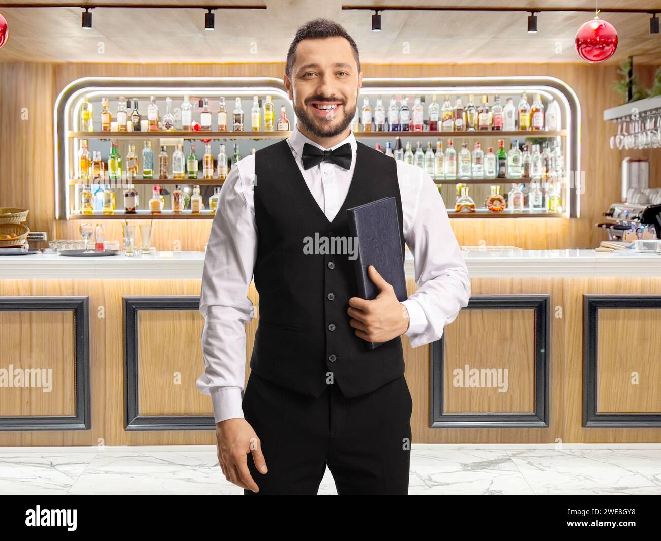 Waiter with a bow tie holding a menu list in a luxury hotel at the bar ...