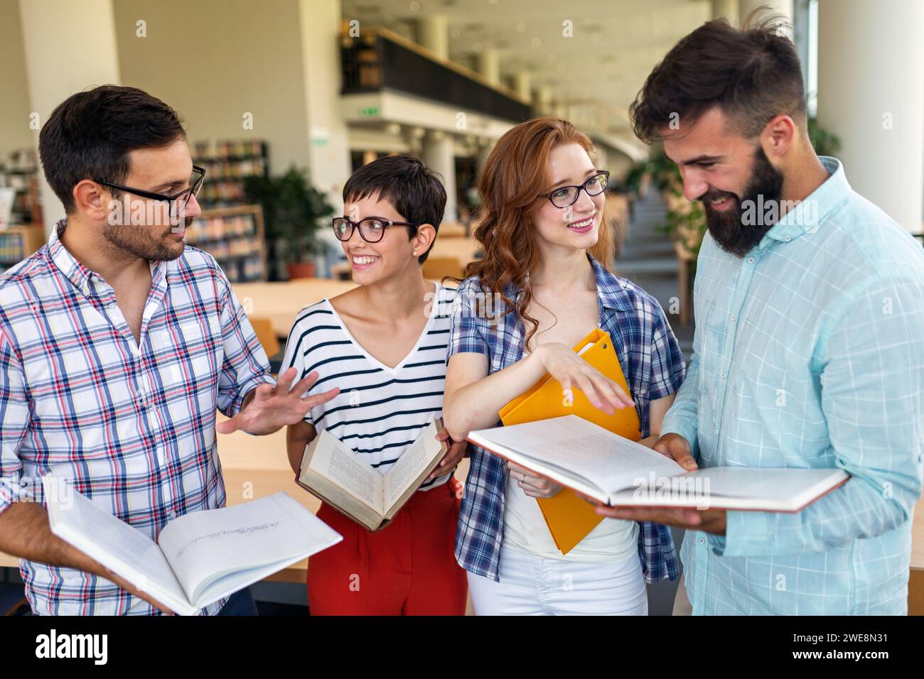 Happy university students studying with books in library. Group of ...