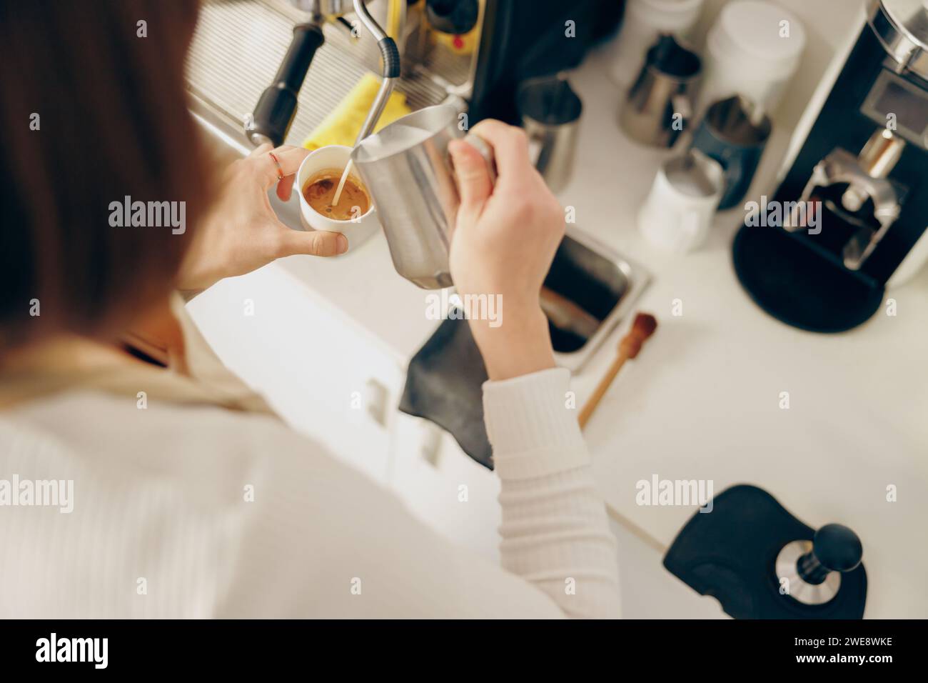 Back view of female barista makes coffee and pours it into a mug while ...