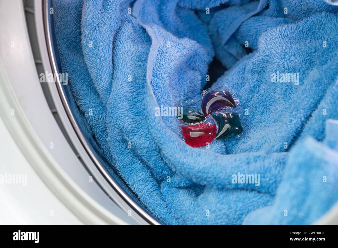 Laundry detergent capsule in washing machine drum on a blue towel ...