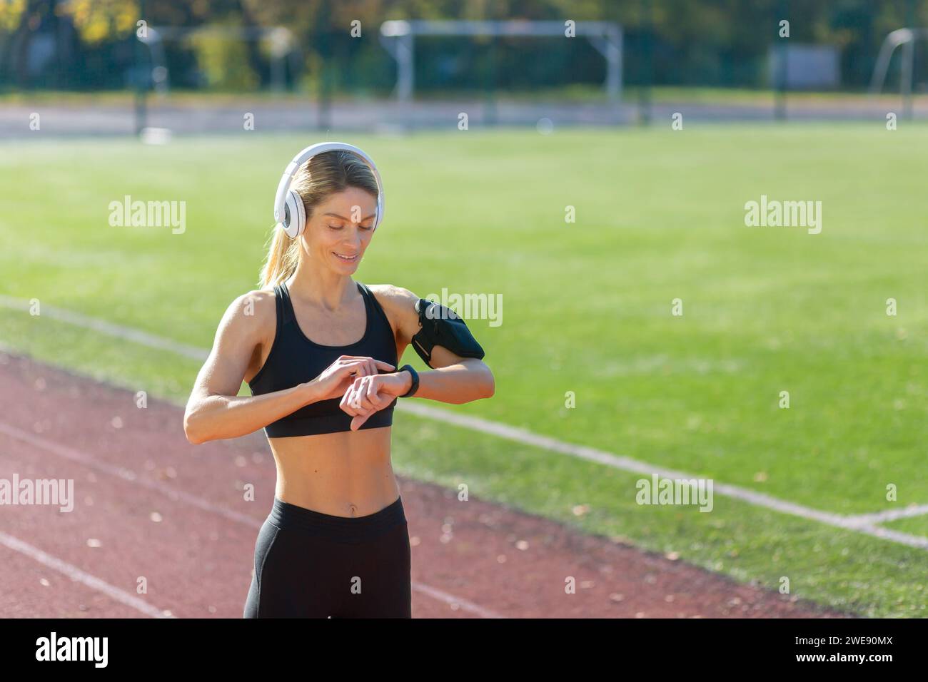 A focused female runner with headphones tunes her workout, checking her ...