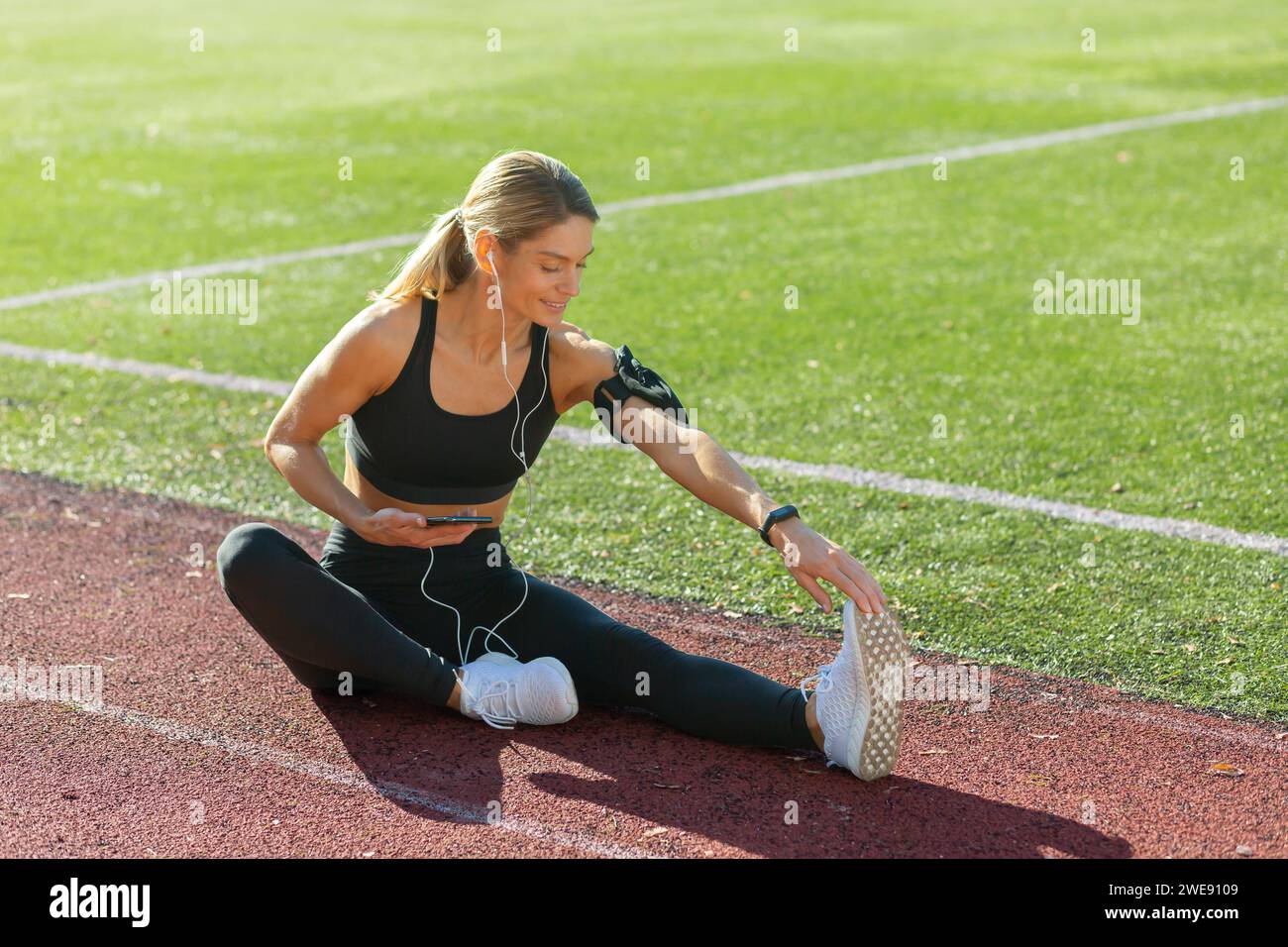 A young female athlete stretching her leg on a track field, enjoying ...