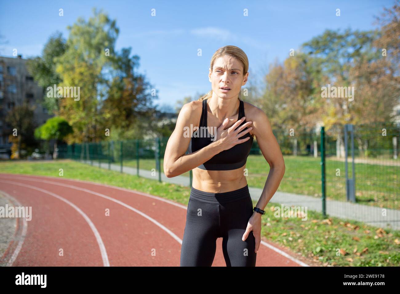 Focused sportswoman taking a break on running track, hands on knees ...
