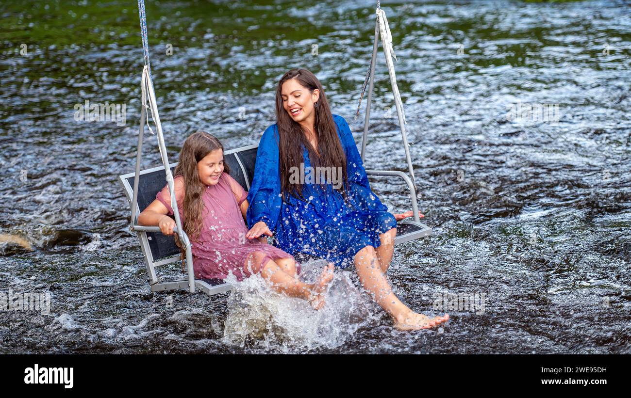 laughing woman and a young girl swing over a fast-flowing river ...