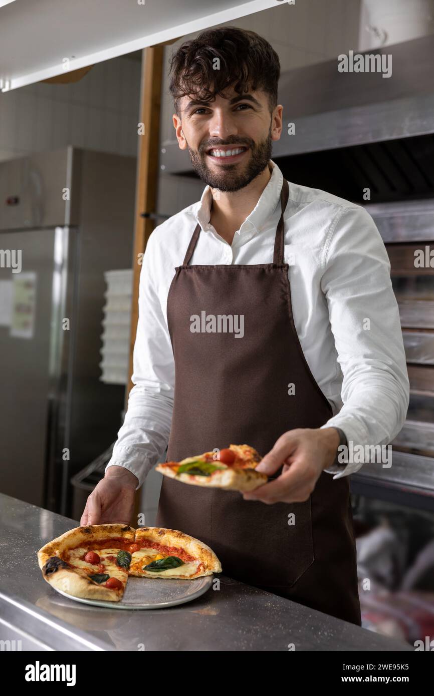 Smiling dark-haired pizzeria worker with pizza slice in hands Stock ...