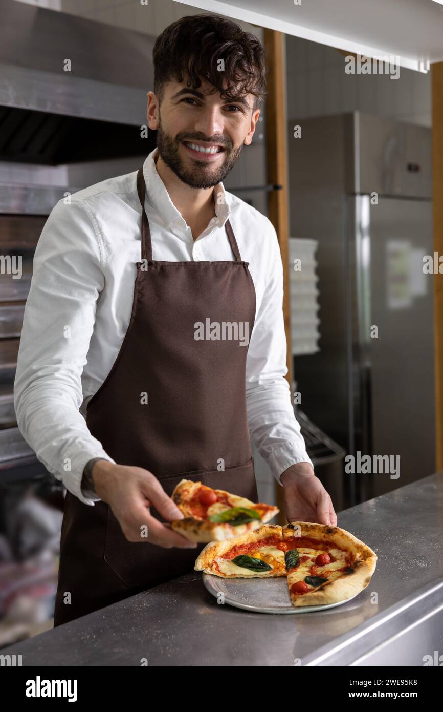Smiling dark-haired pizzeria worker with pizza slice in hands Stock ...