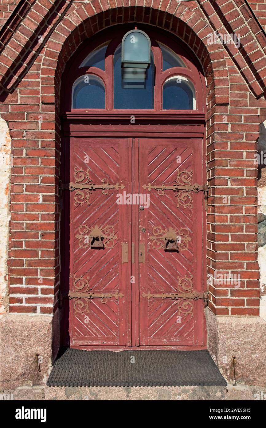 Red door with red brick arch and decorative large metal hinges and ...