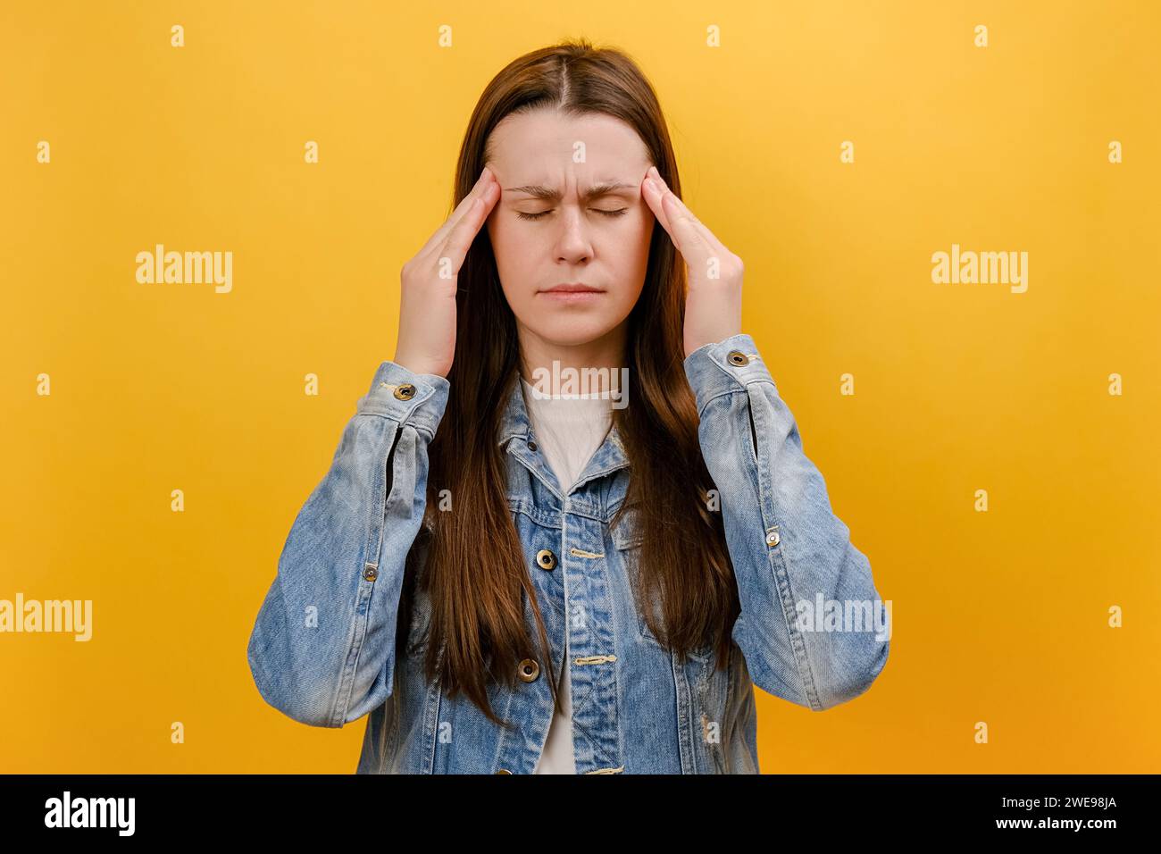 Portrait of tired young woman clasping hands over sore head, frowning ...