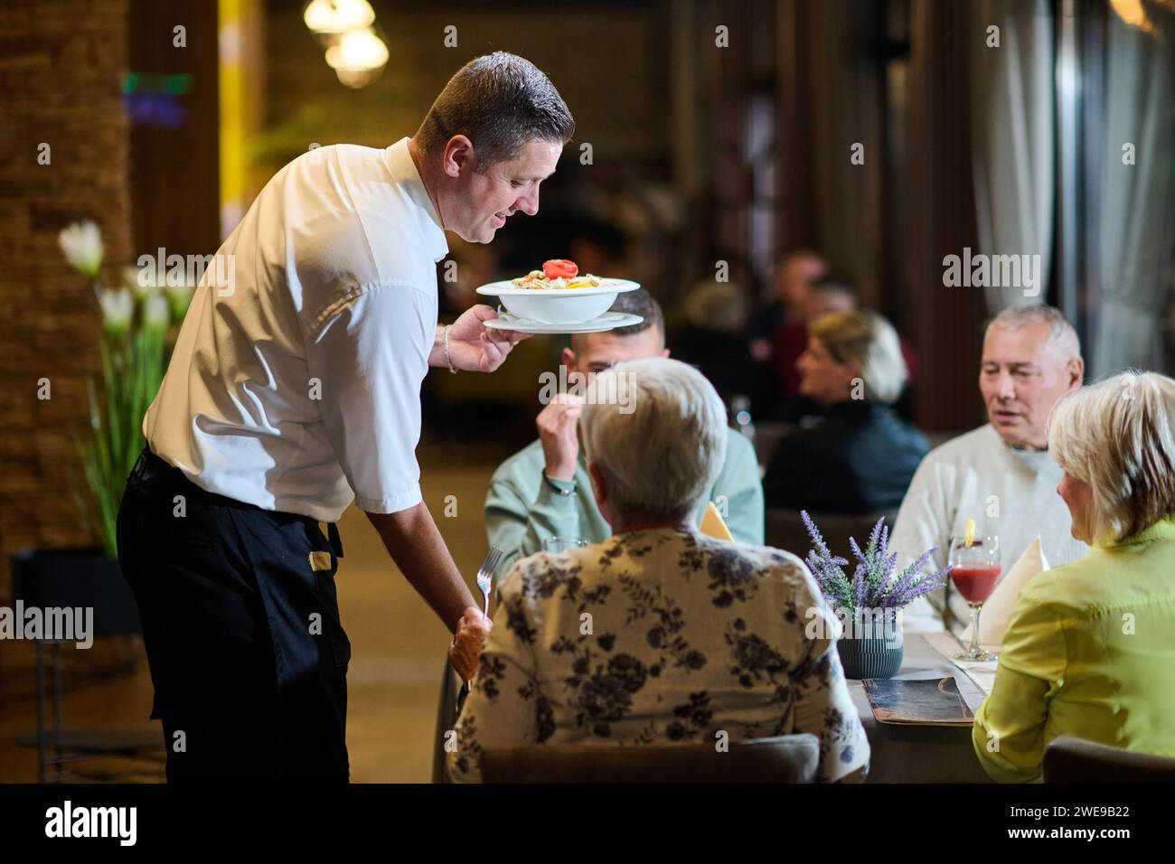 A courteous waiter provides impeccable service to an elderly family and ...
