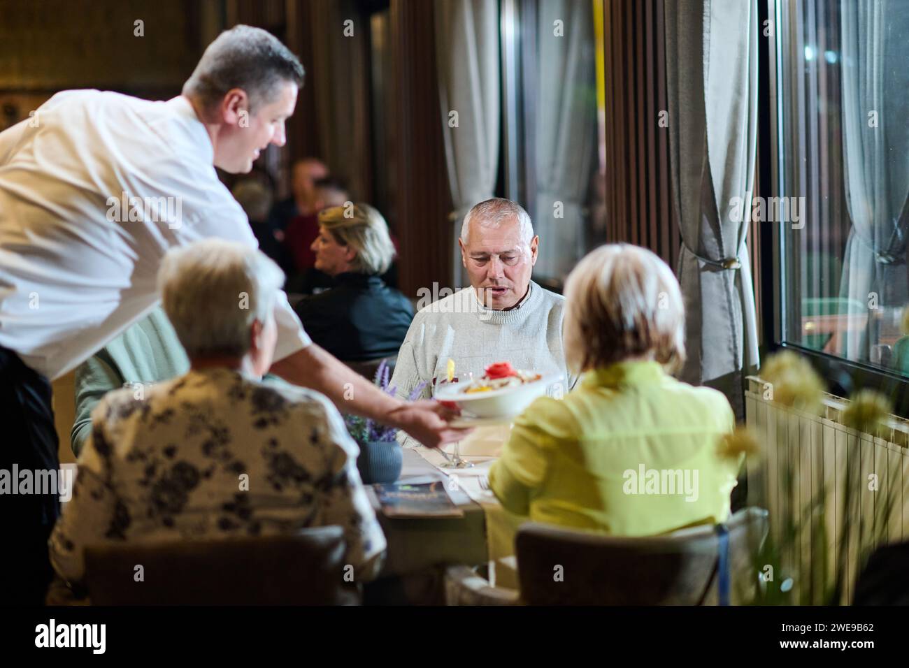 A courteous waiter provides impeccable service to an elderly family and ...