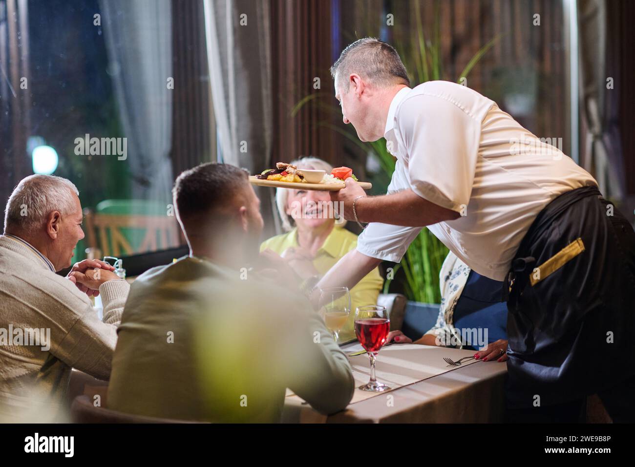 A courteous waiter provides impeccable service to an elderly family and ...