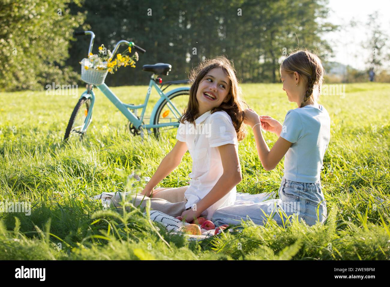 Two Teenage Girls Spend Time On Green Grass Lawn In Park Braid