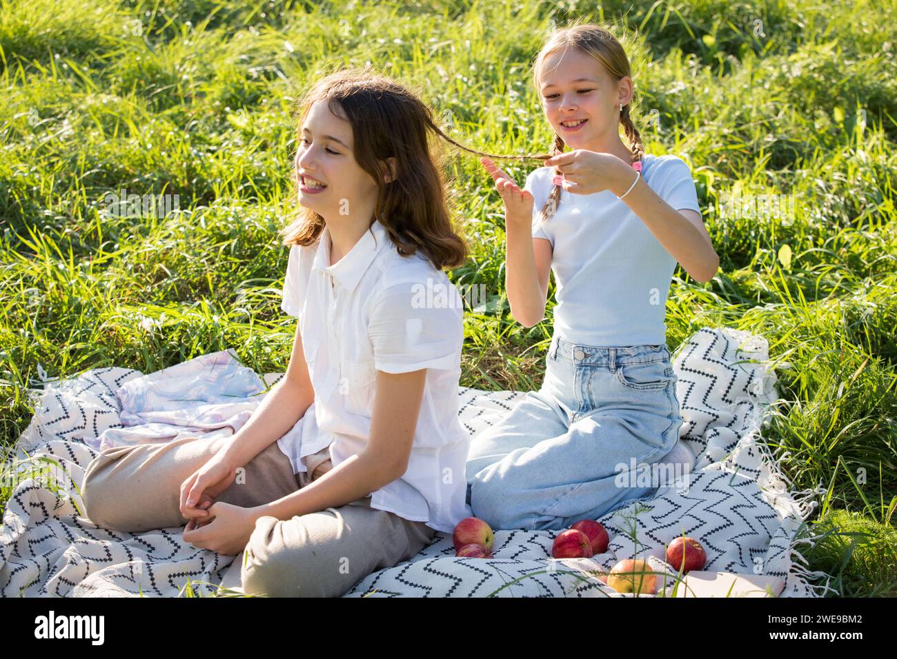 Two Teenage Girls Spend Time On Green Grass Lawn In Park Braid