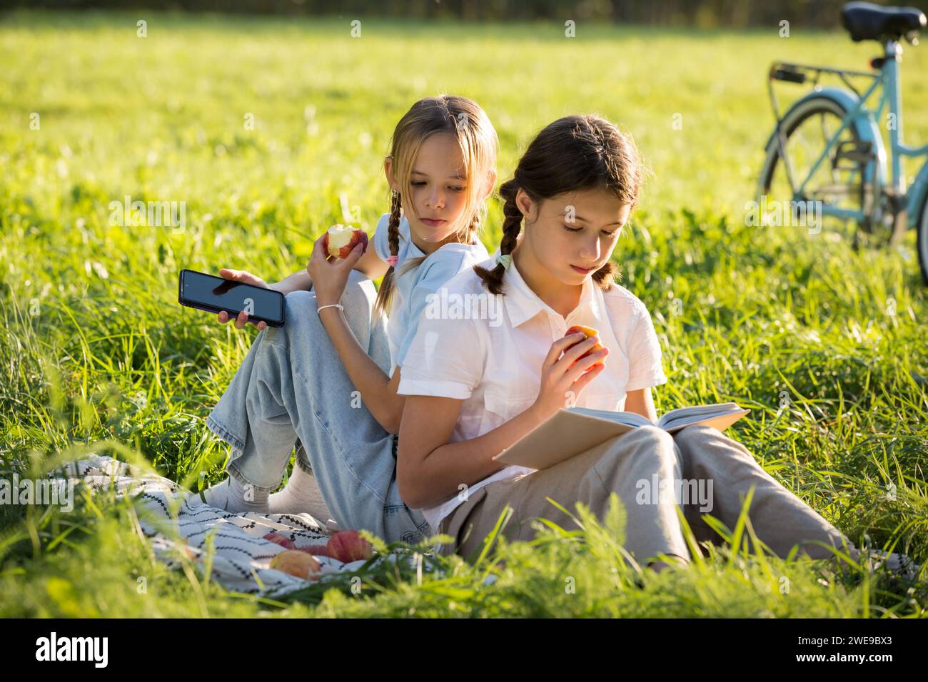 Two Teenage Girls Spend Time On Green Grass Lawn In Park Together One