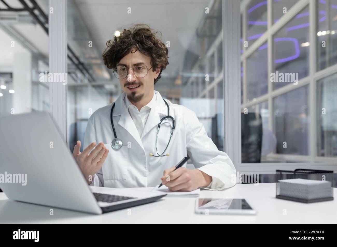A doctor wearing a white lab coat and stethoscope seated in front of a ...