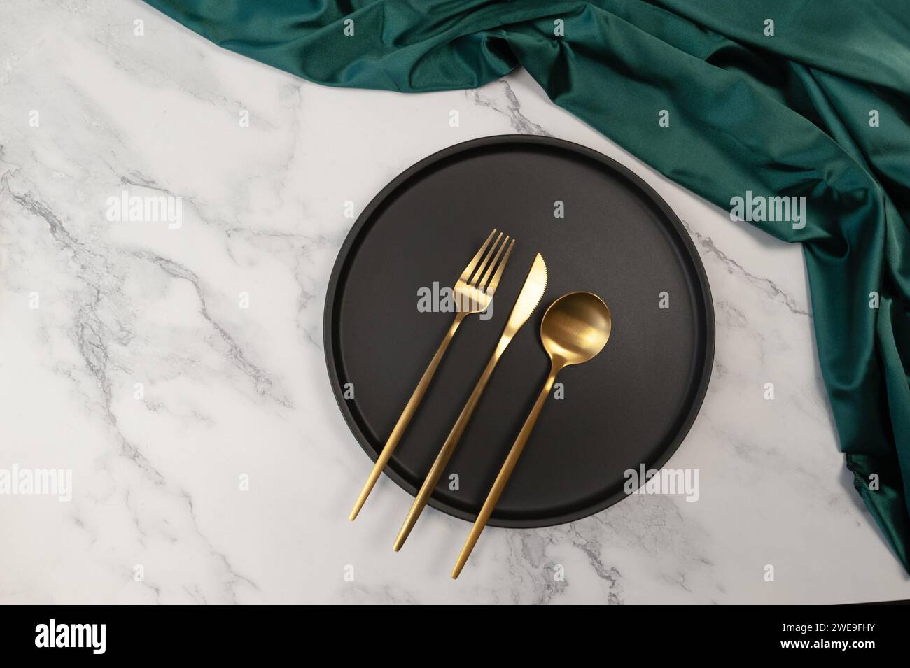 Top view of gold cutlery and black plate on white marble background ...