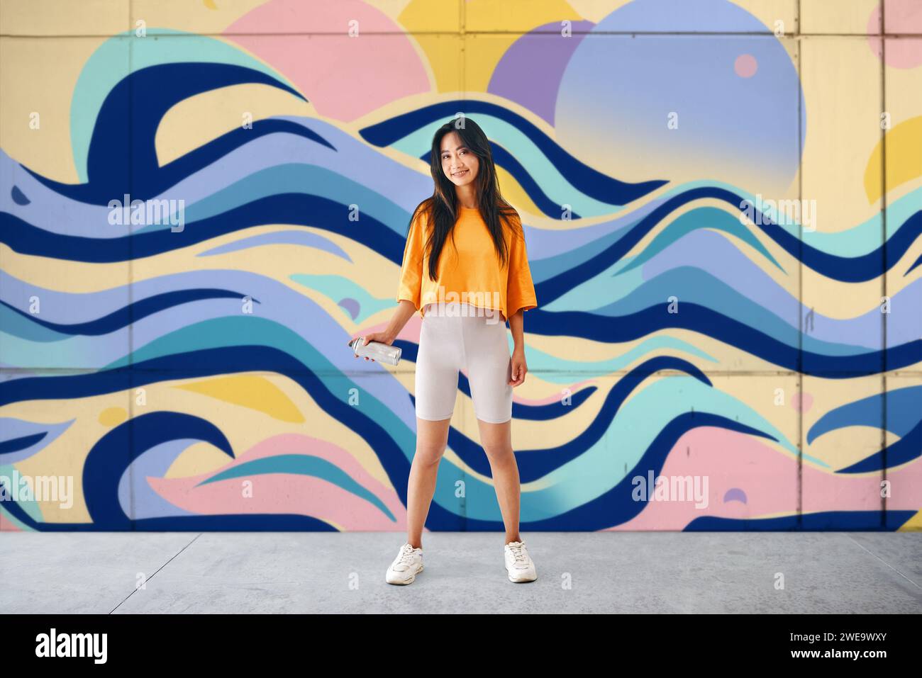 Young female graffiti painter standing near the wall with her paintings ...