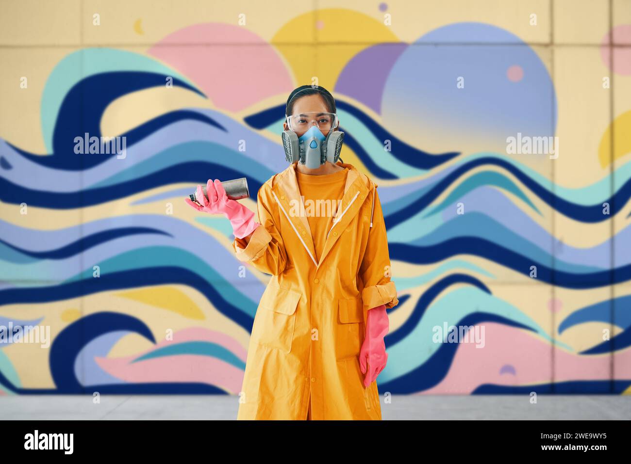 Female graffiti artist in respirator mask standing near the wall with ...