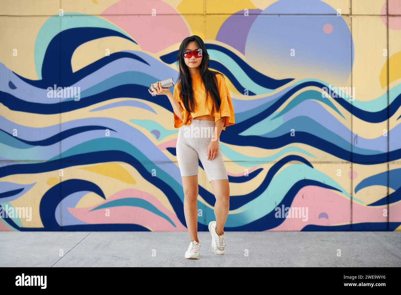 Young female graffiti painter standing near the wall with her paintings ...