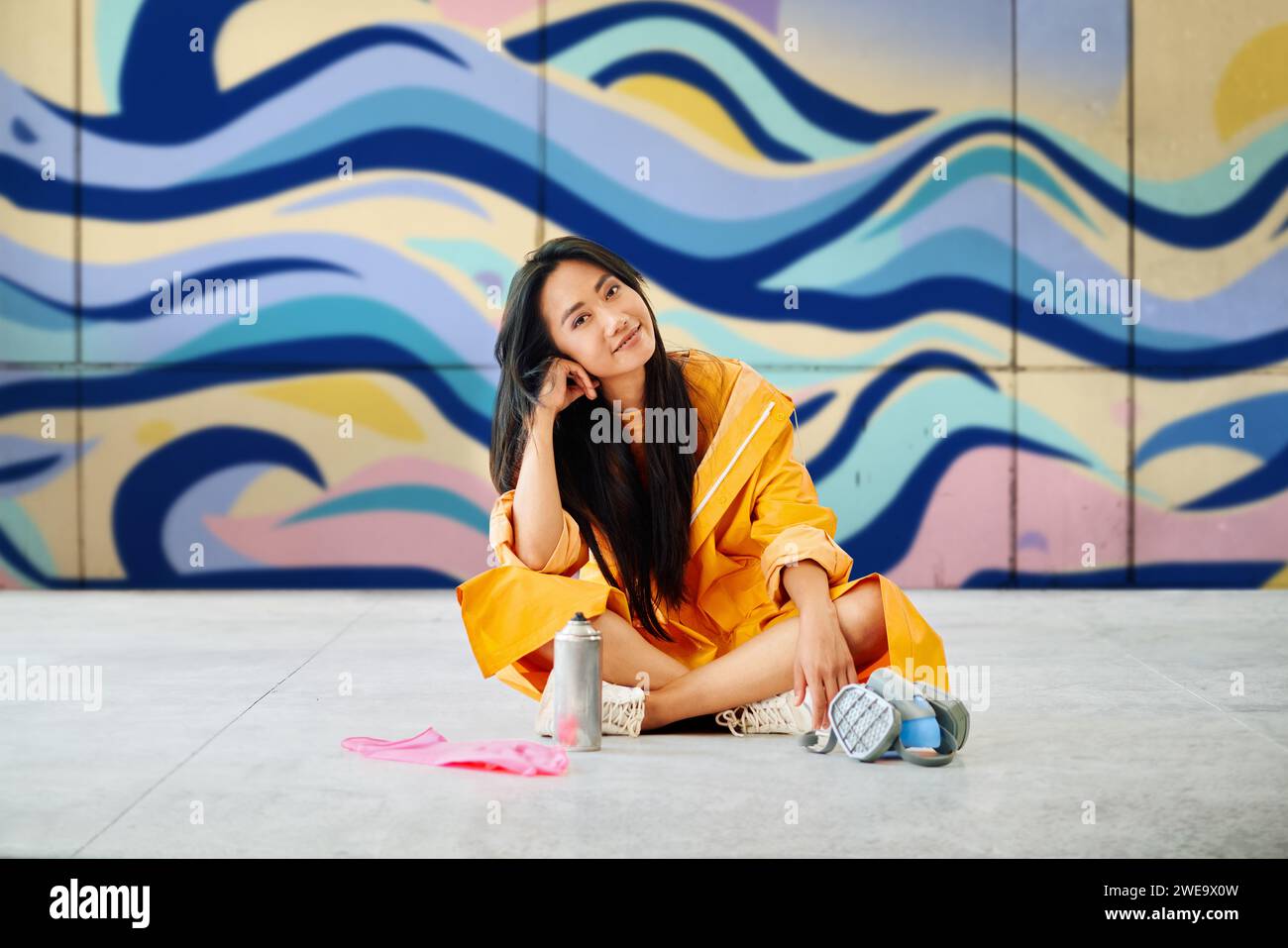 Female street artist rest sitting on the ground near the wall with her ...