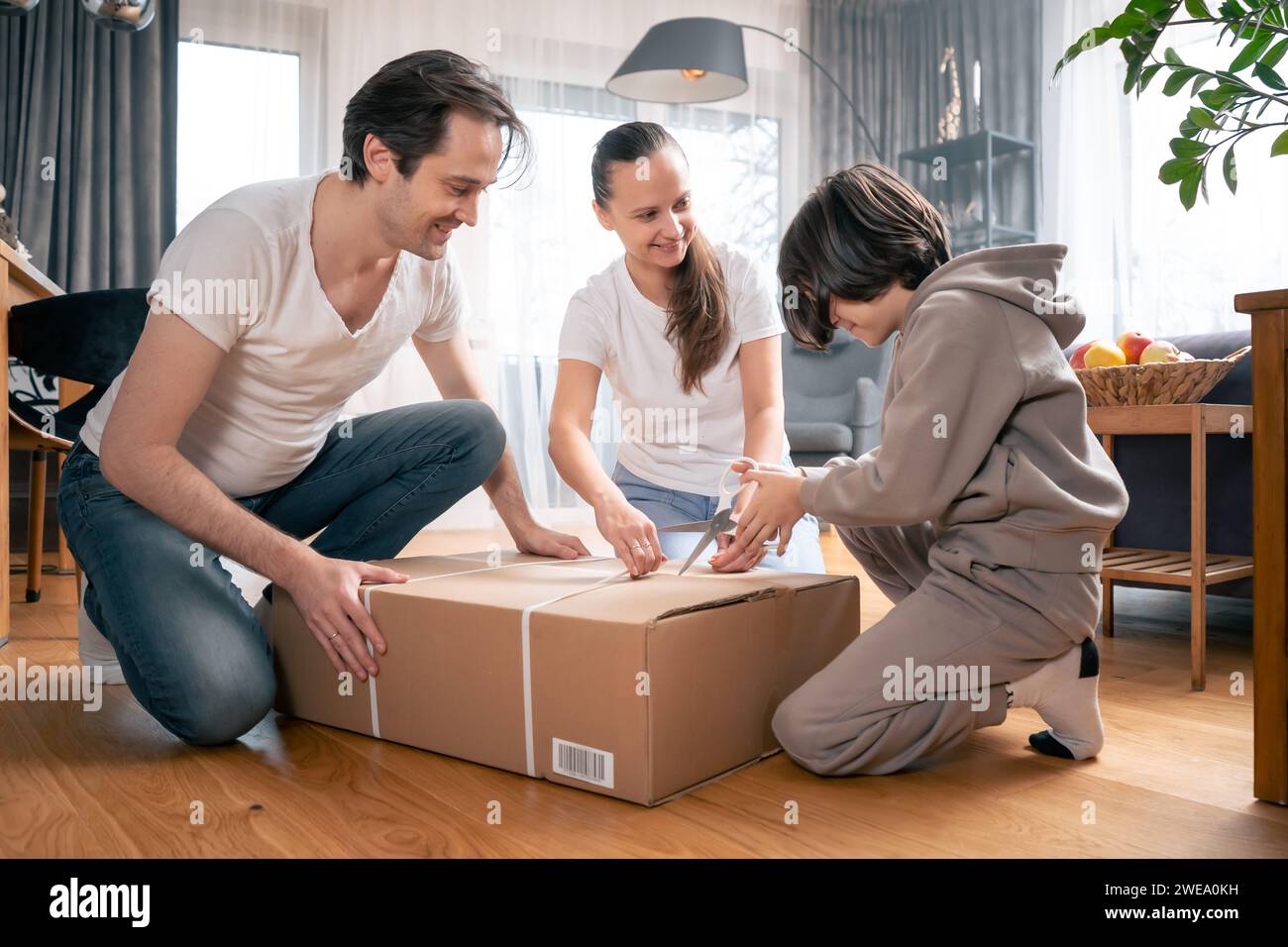 Son, dad and mom, together eagerly unpack a large cardboard box from a ...