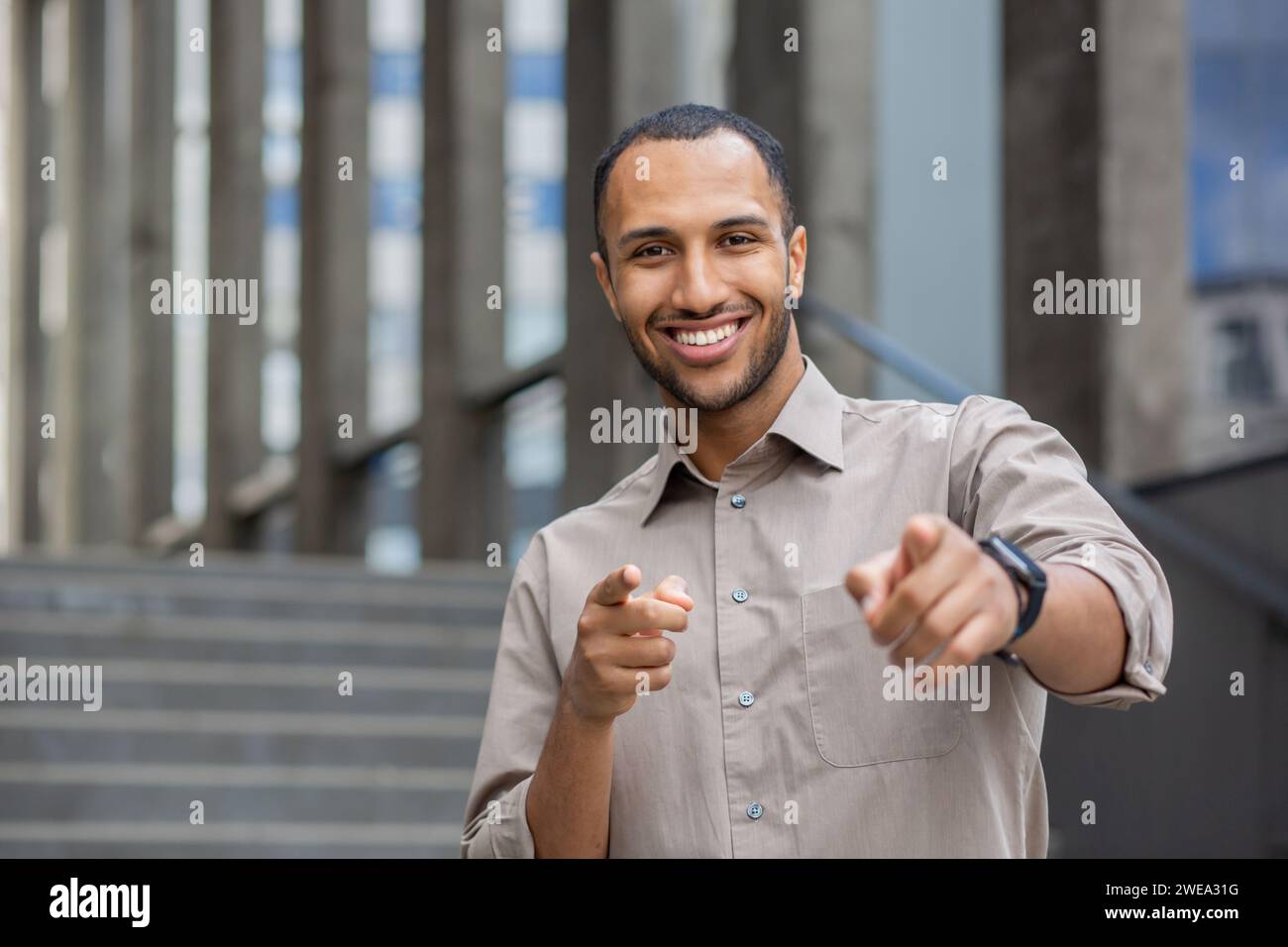 A confident man wearing a watch points directly at the camera, engaging ...