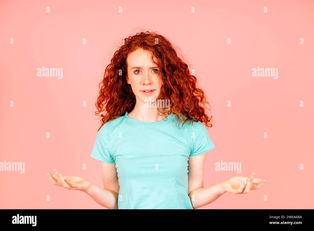 Confused red hair young woman with curly wavy hair spreading hands in ...