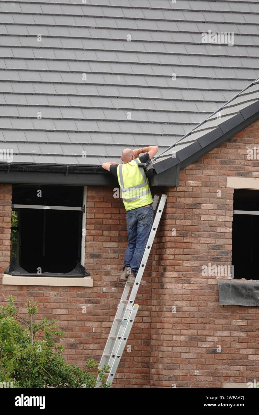 A fitter on a ladder fitting gutttering to the roof of a new house ...