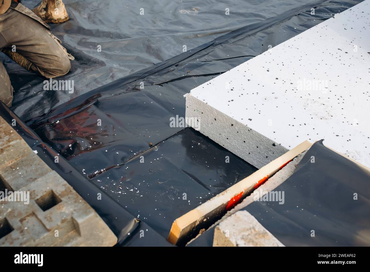 Builder placing polystyrene insulation boards on waterproofing membrane ...
