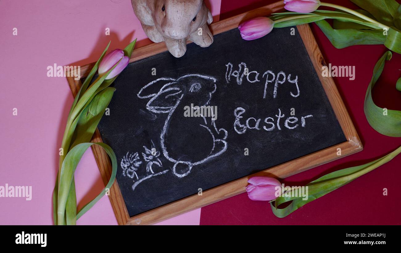 A chalkboard with an easter bunny and Happy Easter on it. Pink tulips ...