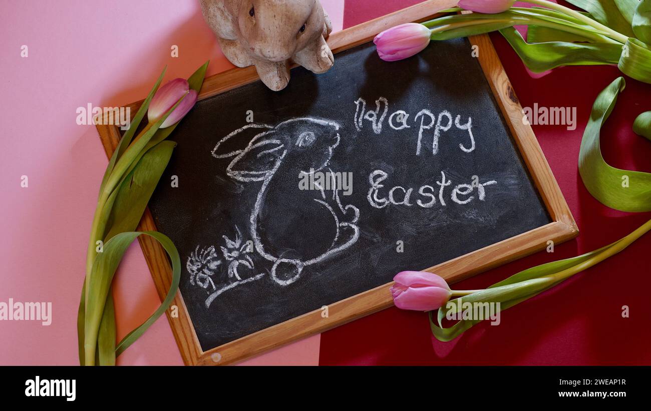 A chalkboard with an easter bunny and Happy Easter on it. Pink tulips ...