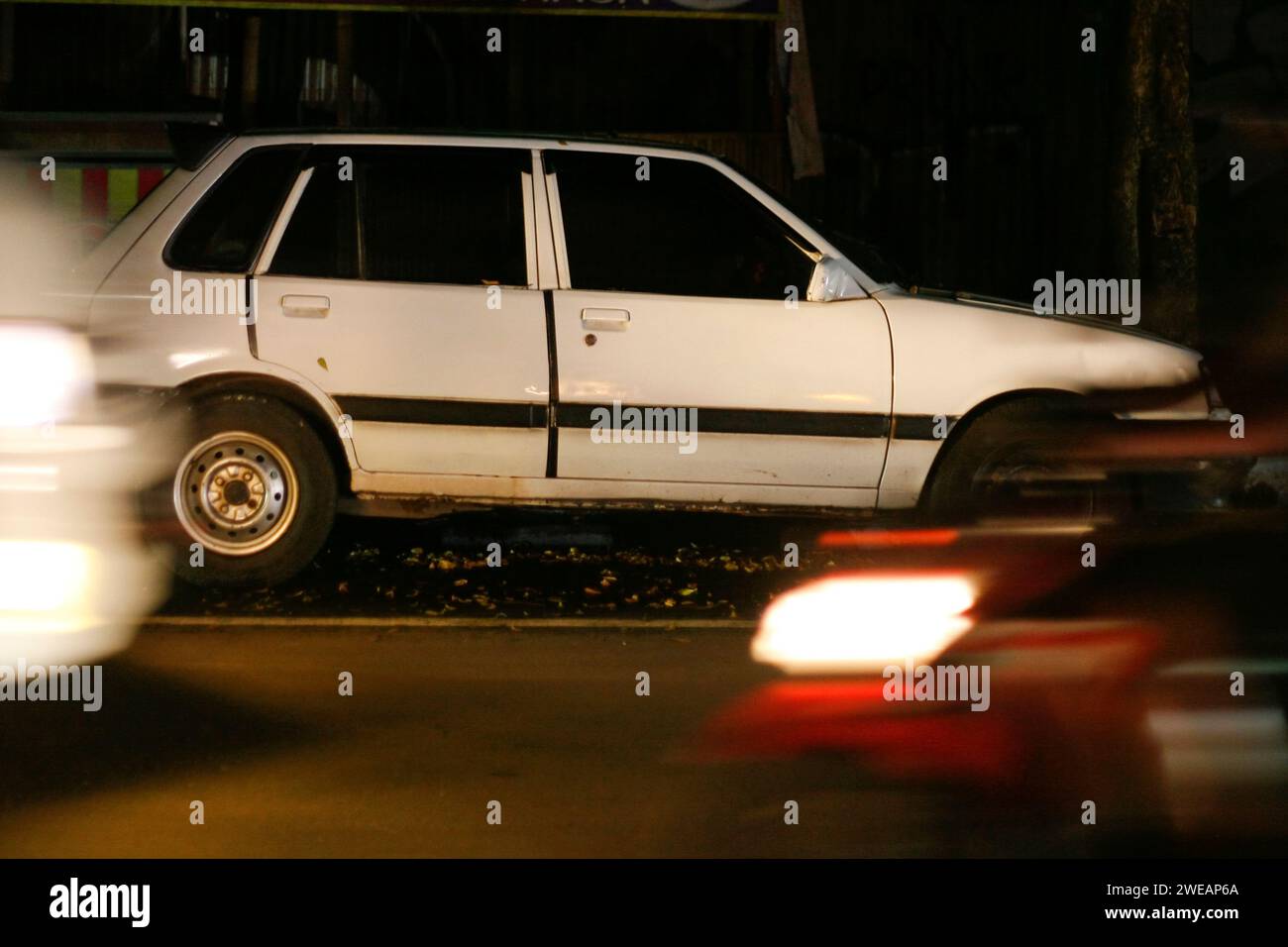 white hatchback car parked on the side of the road at night Stock Photo ...