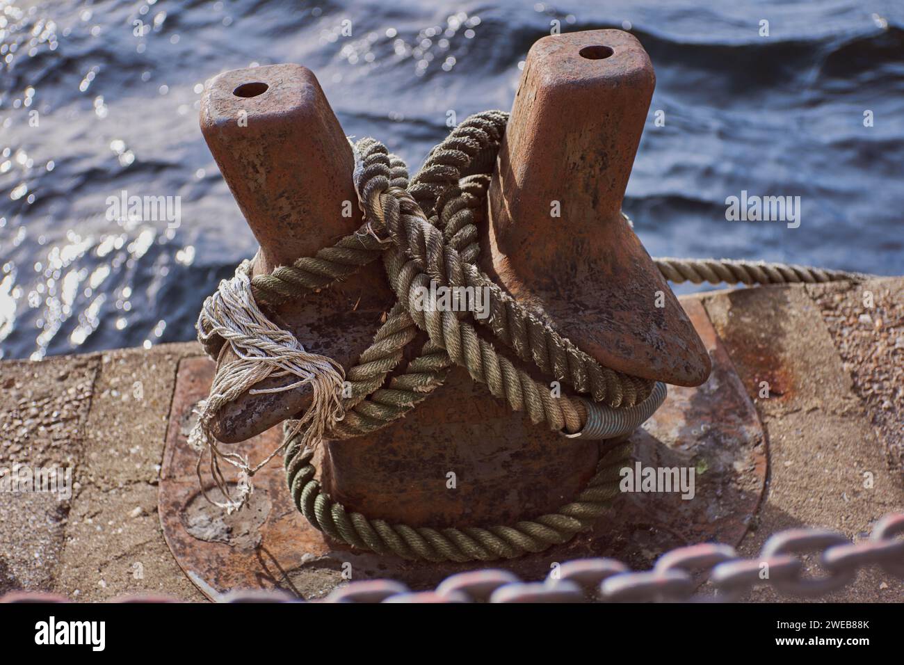 A rusty Double Bitt Bollard, wrapped in Mooring lines (ropes) and a ...