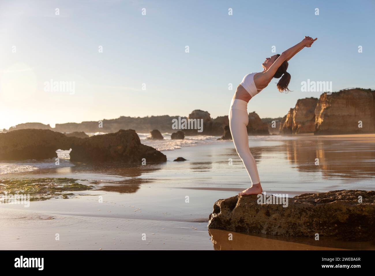 woman standing on rocks by the sea doing a backbend, yoga pose Stock ...