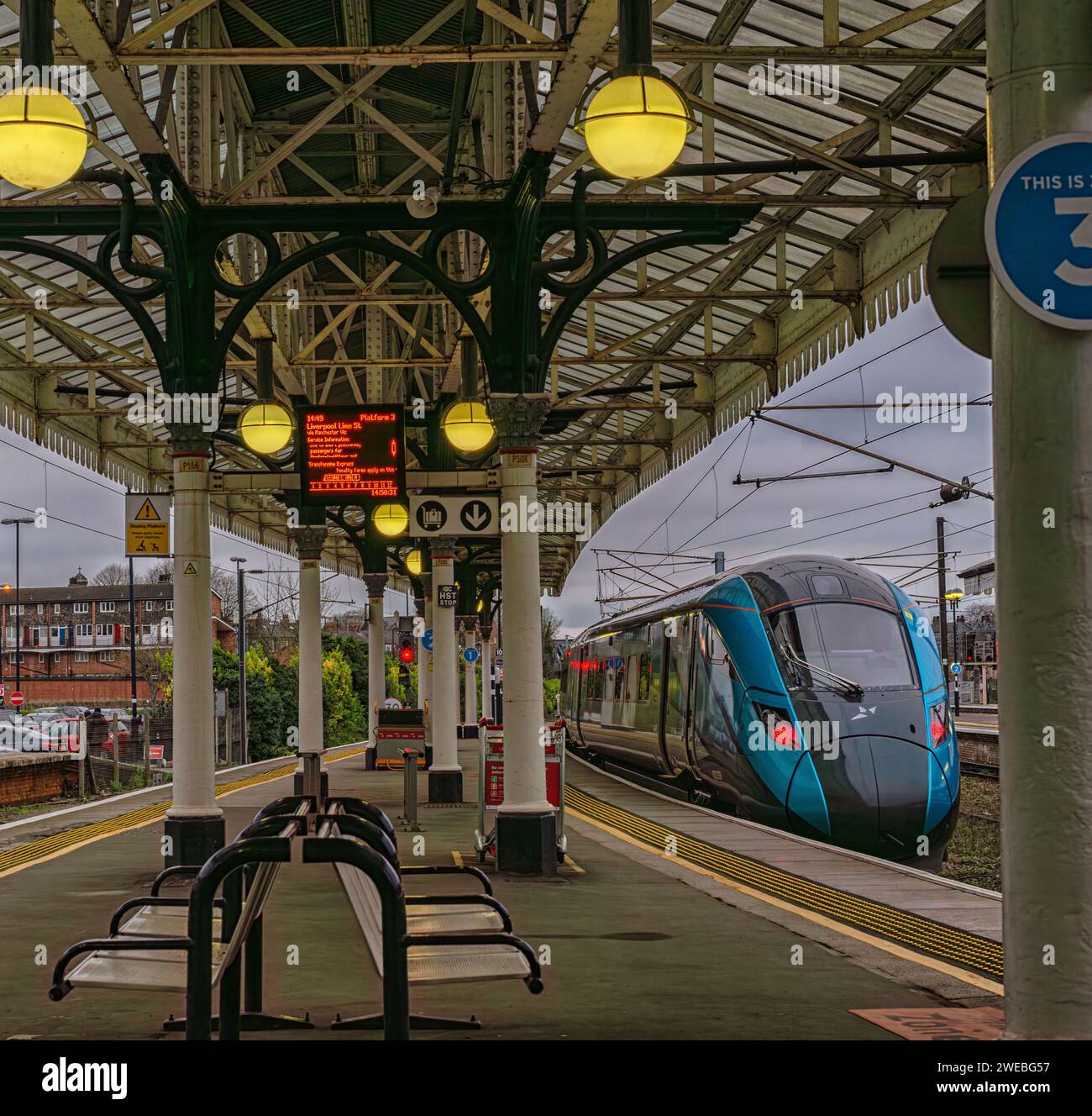 A train departs a station in an evening light. Lamps under a 19th ...