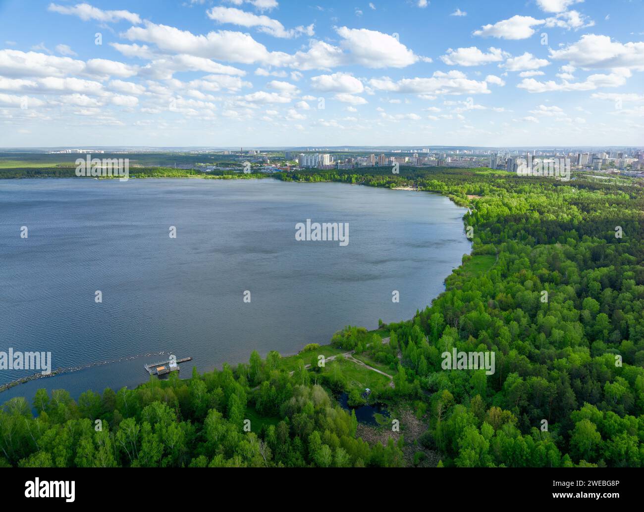 Big lake with green shores in bright sun light and city on horizon ...