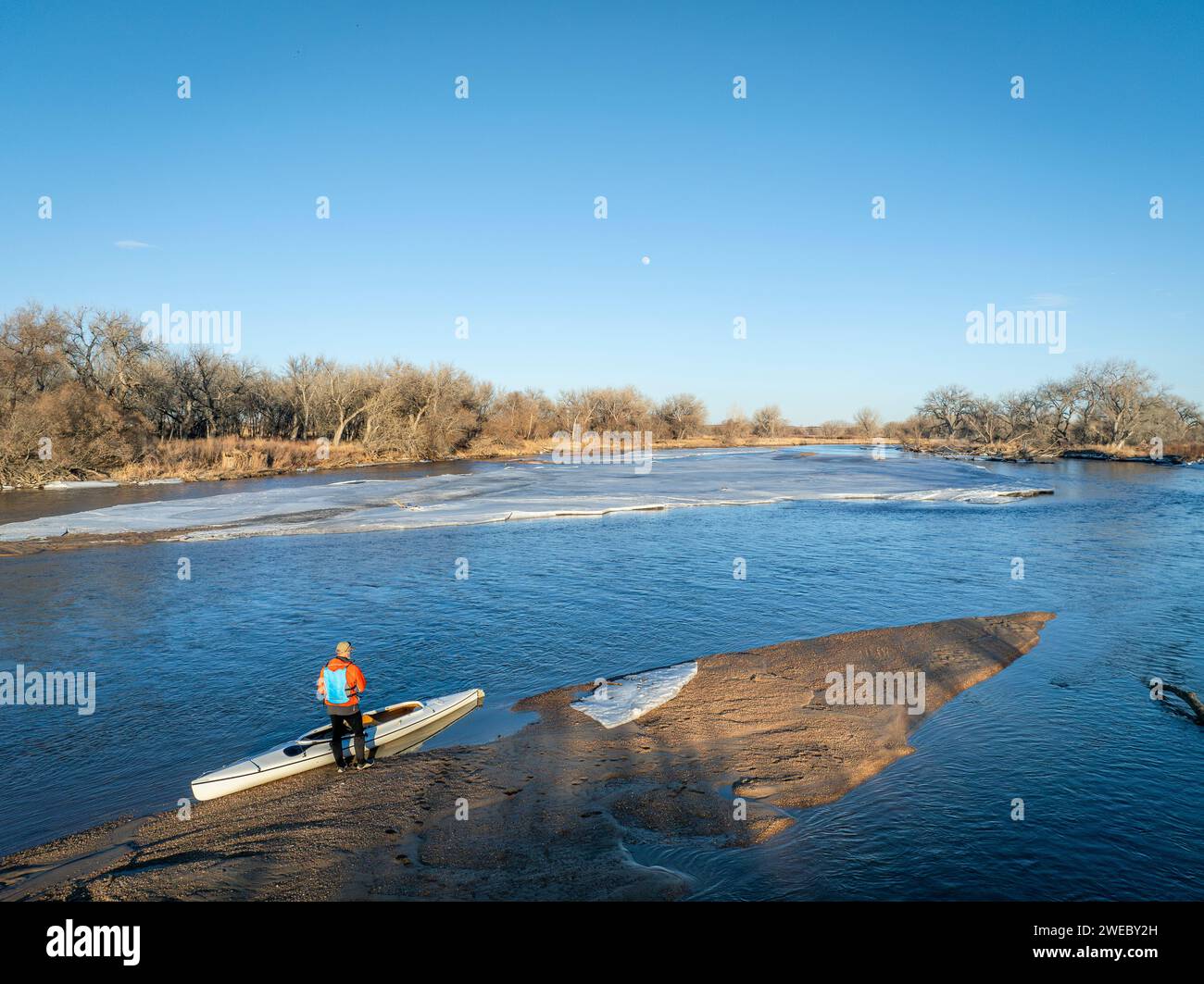 male paddler with a decked expedition canoe on a sandbar with ice floe ...