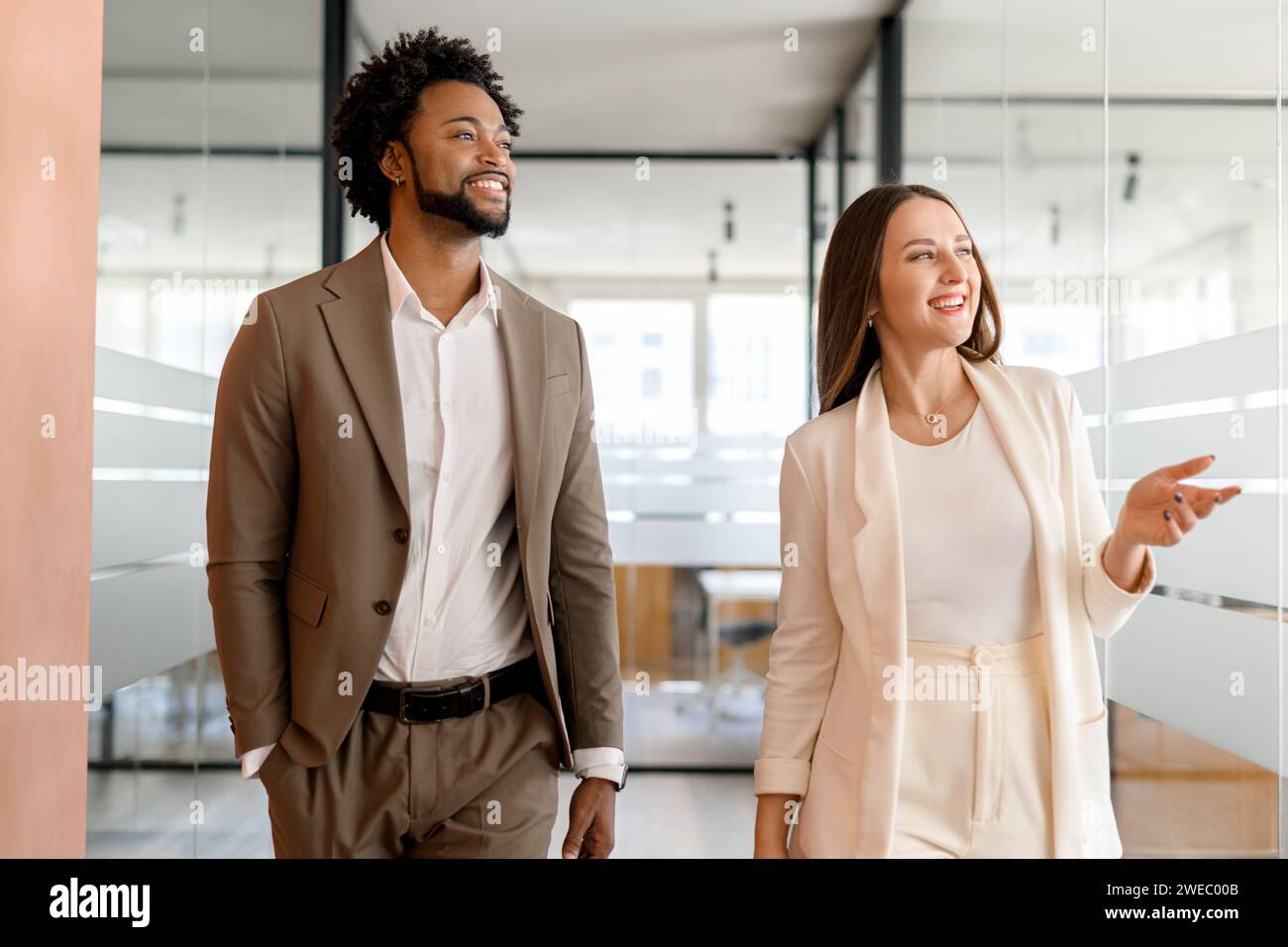 In a light-filled office, a man and woman walk together, engaging in a ...