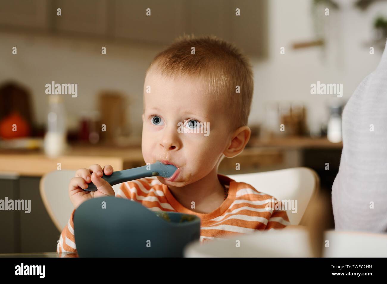 Adorable baby boy with blond hair and blue eyes putting spoon into ...