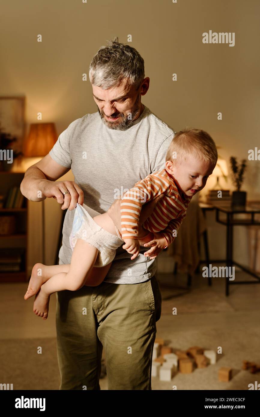 Mature disgusted father in casualwear holding his adorable baby son on ...