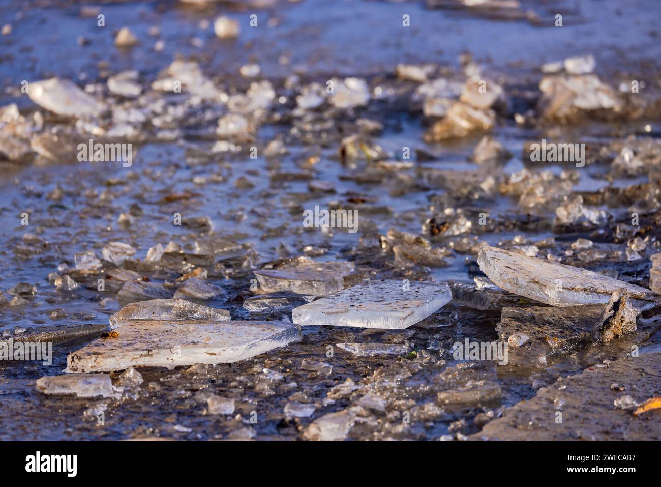 Pieces of ice on a dirt road with splinters and broken ice in climate ...