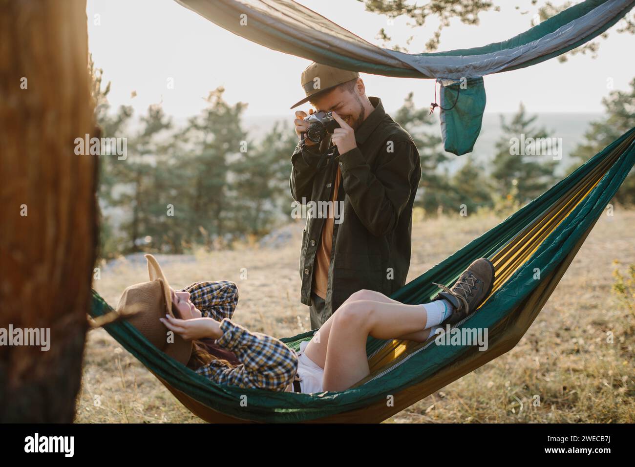 Couple having fun relaxing in hammocks outdoors. A guy takes a picture ...