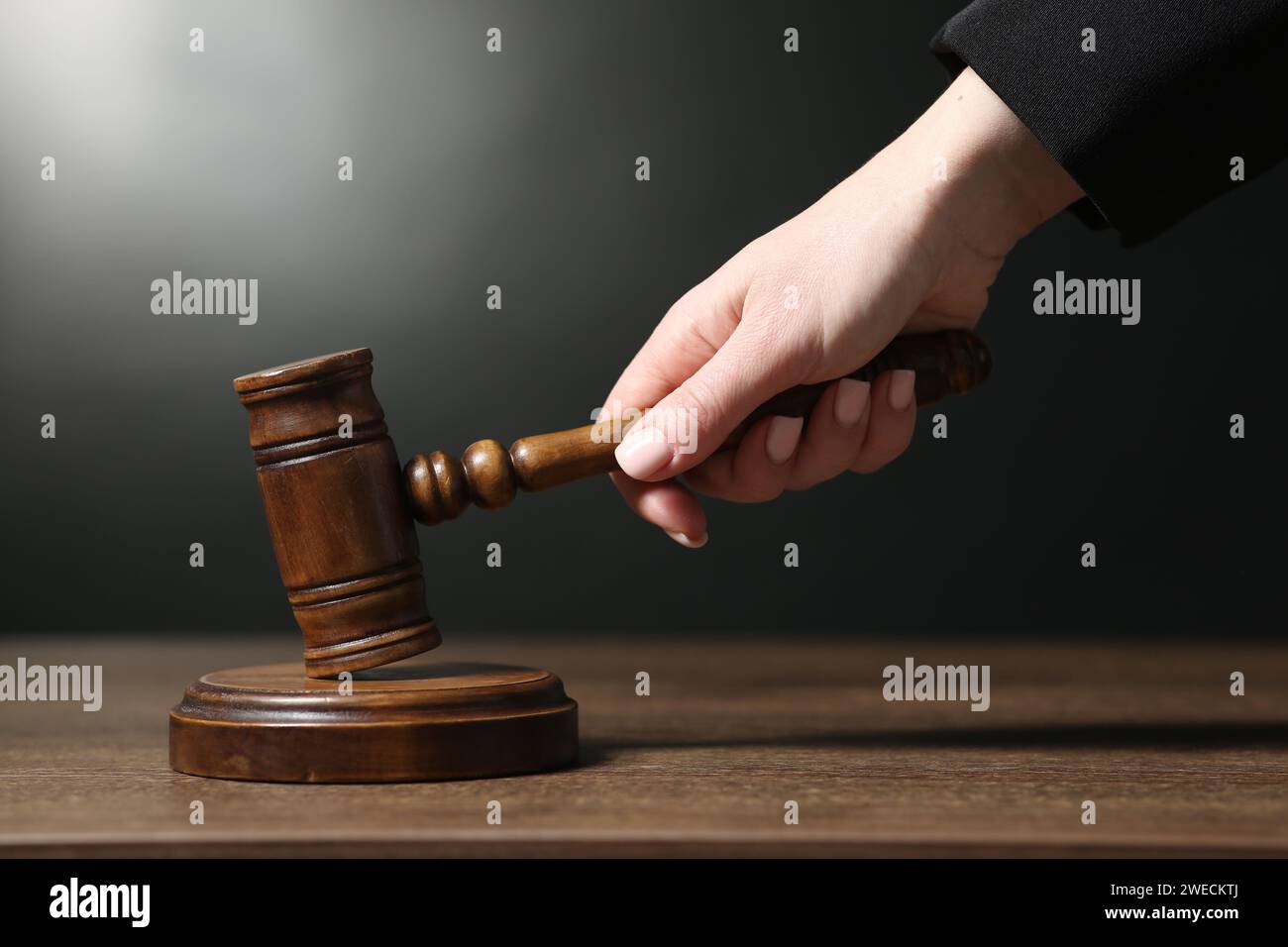 Judge striking mallet at wooden table against dark background, closeup ...