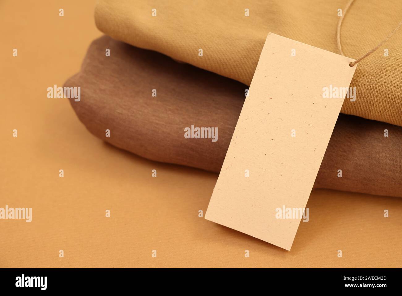 Garment with cardboard tag on kraft paper sheet, closeup. Space for ...