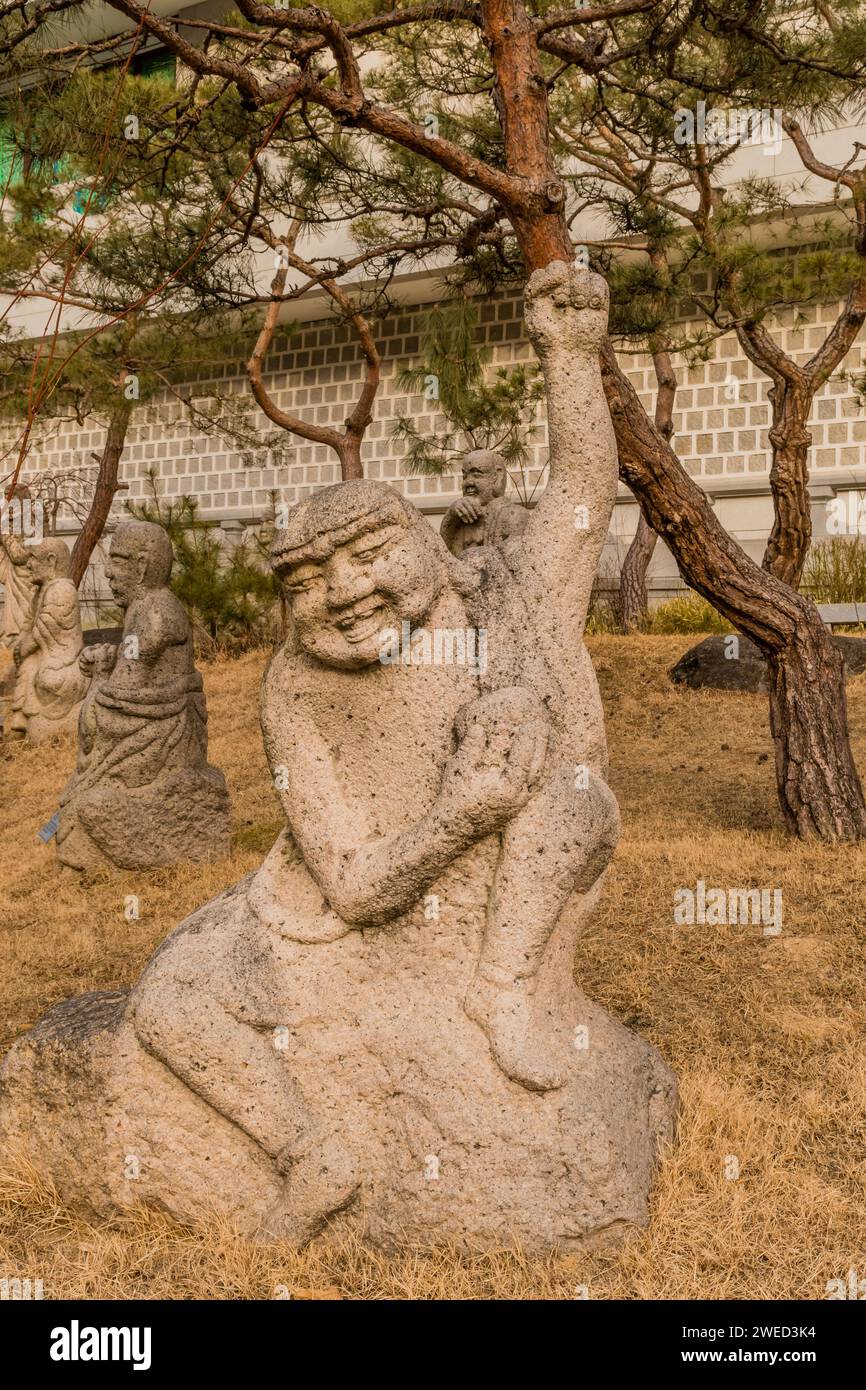 Stone carved statue of Buddhist deity in front of white wall in garden ...