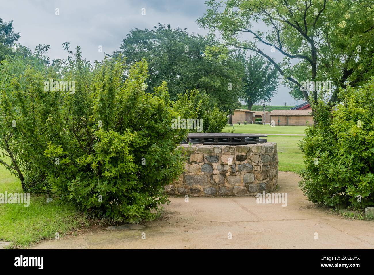 Side view of old stone water well with wooden cover in public park in ...
